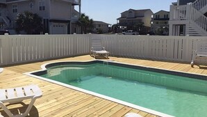 Piscina com deck de madeira, cadeiras de lounge brancas e cerca branca.