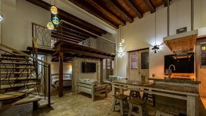 Um interior rústico com piso de pedra, escada de madeira, área de jantar com banquetas, cozinha com pia e uma TV fixada em uma parede de pedra.