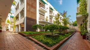 Um pátio com caminho de tijolos, plantas verdes e um edifício moderno com sacadas.