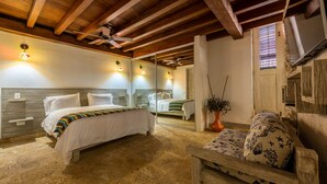 Quarto com teto de madeira, cama com manta listrada, mesa de cabeceira, espelho, planta em vaso e janela com persianas.