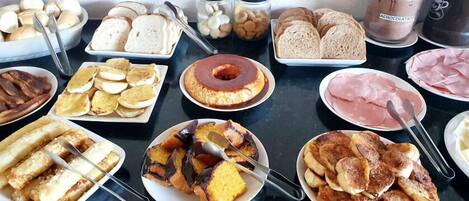 Um buffet de café da manhã com diversos pratos, incluindo pães, doces e carnes.