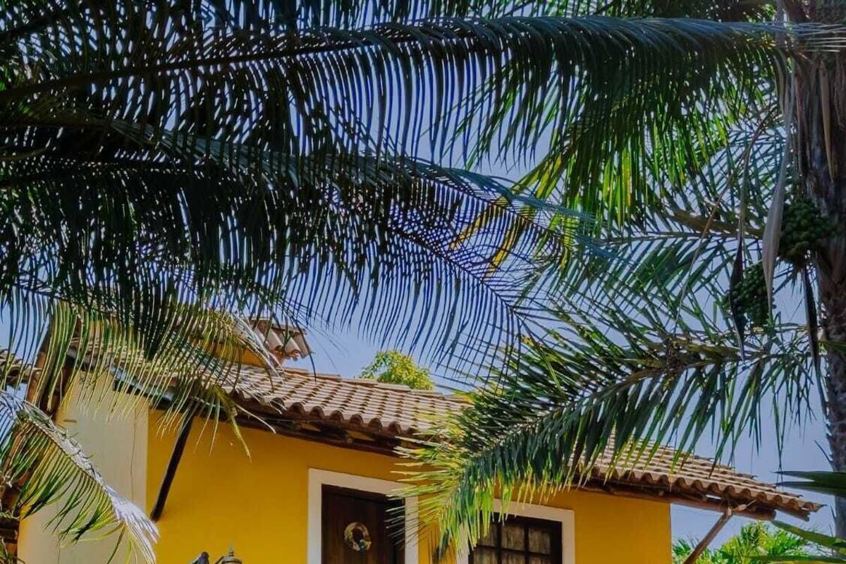 Um edifício amarelo com telhado de azulejos, porta de madeira e escadaria que leva à entrada.