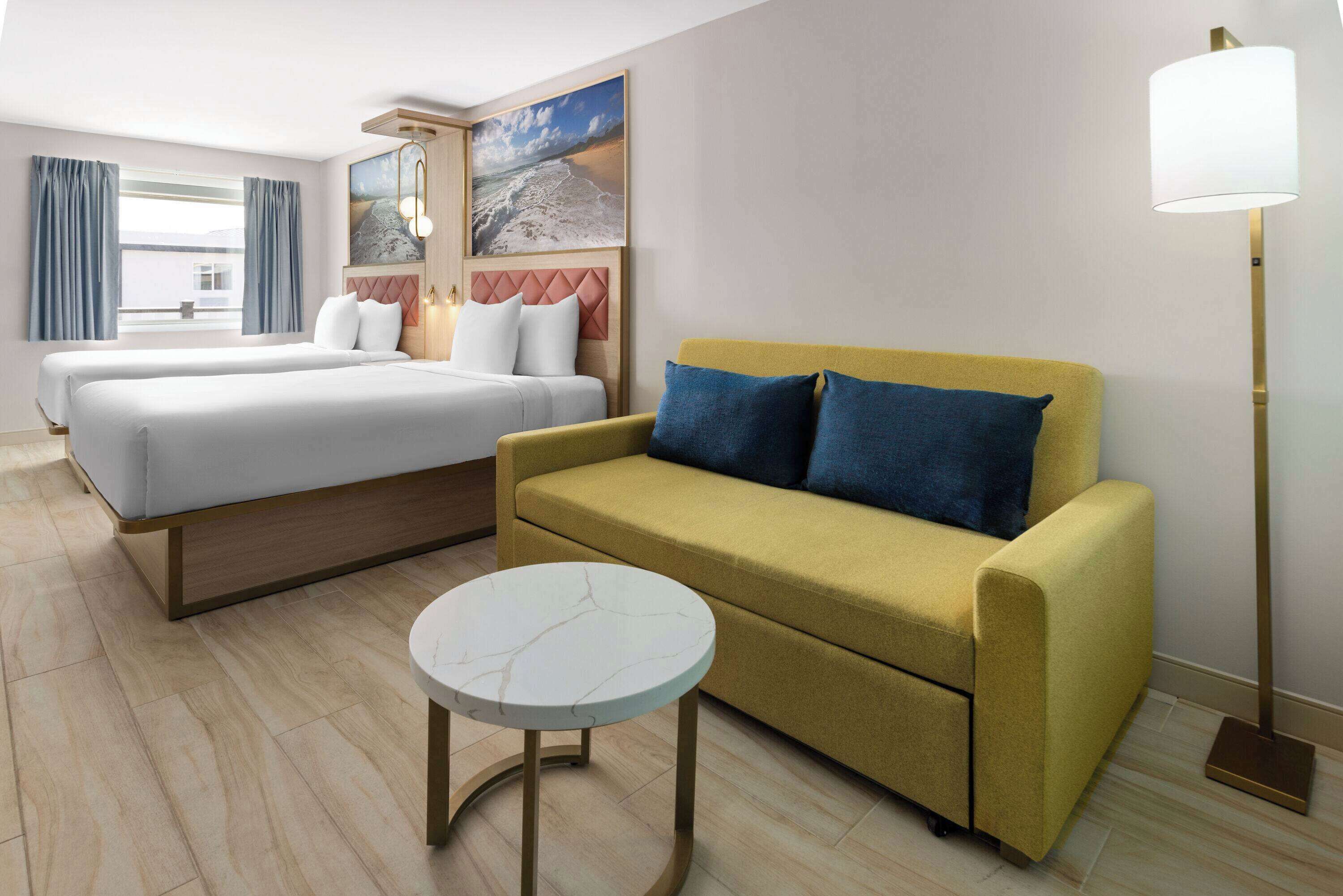 Quarto de hotel com duas camas, um sofá, uma mesa redonda pequena e um quadro na parede.