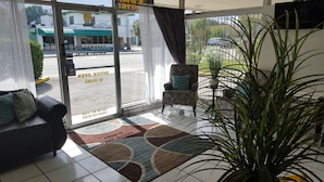 Um saguão de hotel com área de estar, uma janela grande com vista para a rua e um letreiro de um bar próximo.