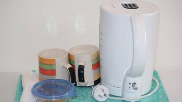 Uma cafeteira branca, duas chávenas com riscas, um recipiente azul e um guardanapo branco sobre uma bancada verde.
