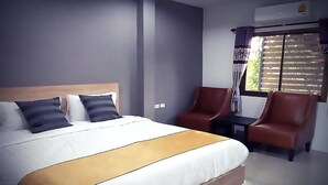 Quarto de hotel com uma cama grande, duas cadeiras, uma mesinha e uma janela com cortinas.