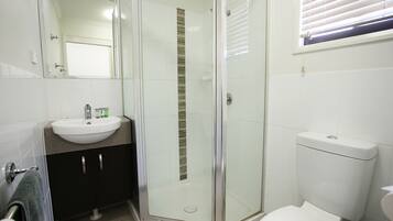 Uma casa de banho moderna com cabine de duche em vidro, lavatório branco e sanita.