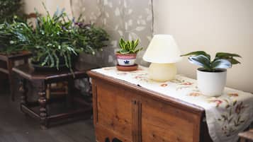 Um armário de madeira com toalha de mesa florida, uma luminária branca e duas plantas em vasos.