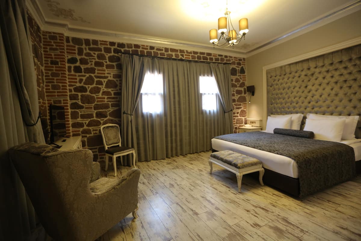 Quarto com uma cama grande, uma cadeira, uma escrivaninha e uma parede de pedra.