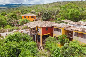 Um edifício de vários andares com fachada vermelha e amarela, várias varandas e um pátio com mesas ao ar livre.