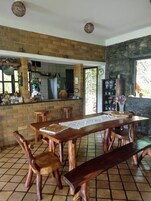 Uma cozinha rústica com uma longa mesa de madeira, cadeiras e uma parede de tijolos.