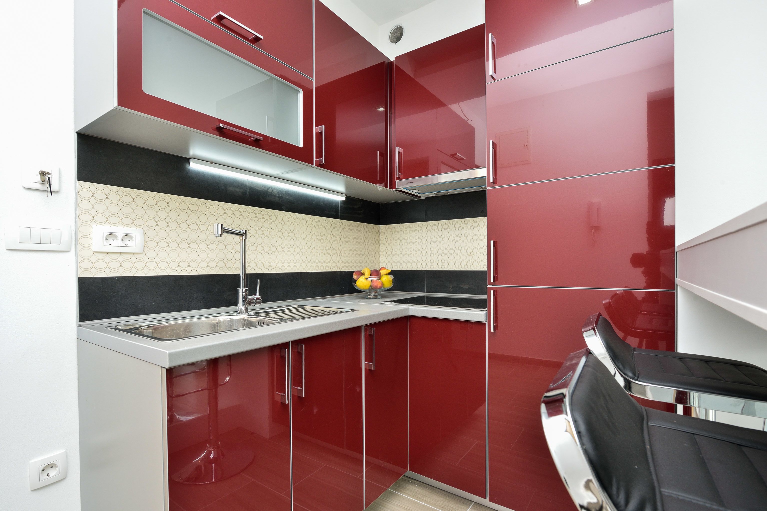 Uma cozinha compacta com armários vermelhos, uma pia de aço inoxidável e bancada preta.