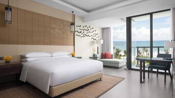 Quarto de hotel moderno com uma cama grande, uma mesa de trabalho e uma varanda com vista para o oceano.