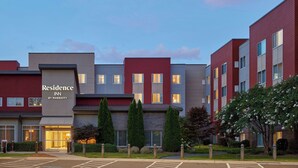 Um hotel com vários andares e um destaque para a placa 'Residence Inn by Marriott', apresentando um design arquitetônico moderno com fachadas em vermelho e cinza, e um estacionamento em frente.