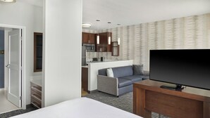 Quarto de hotel com cama, televisão, sofá, cozinha e guarda-roupa.