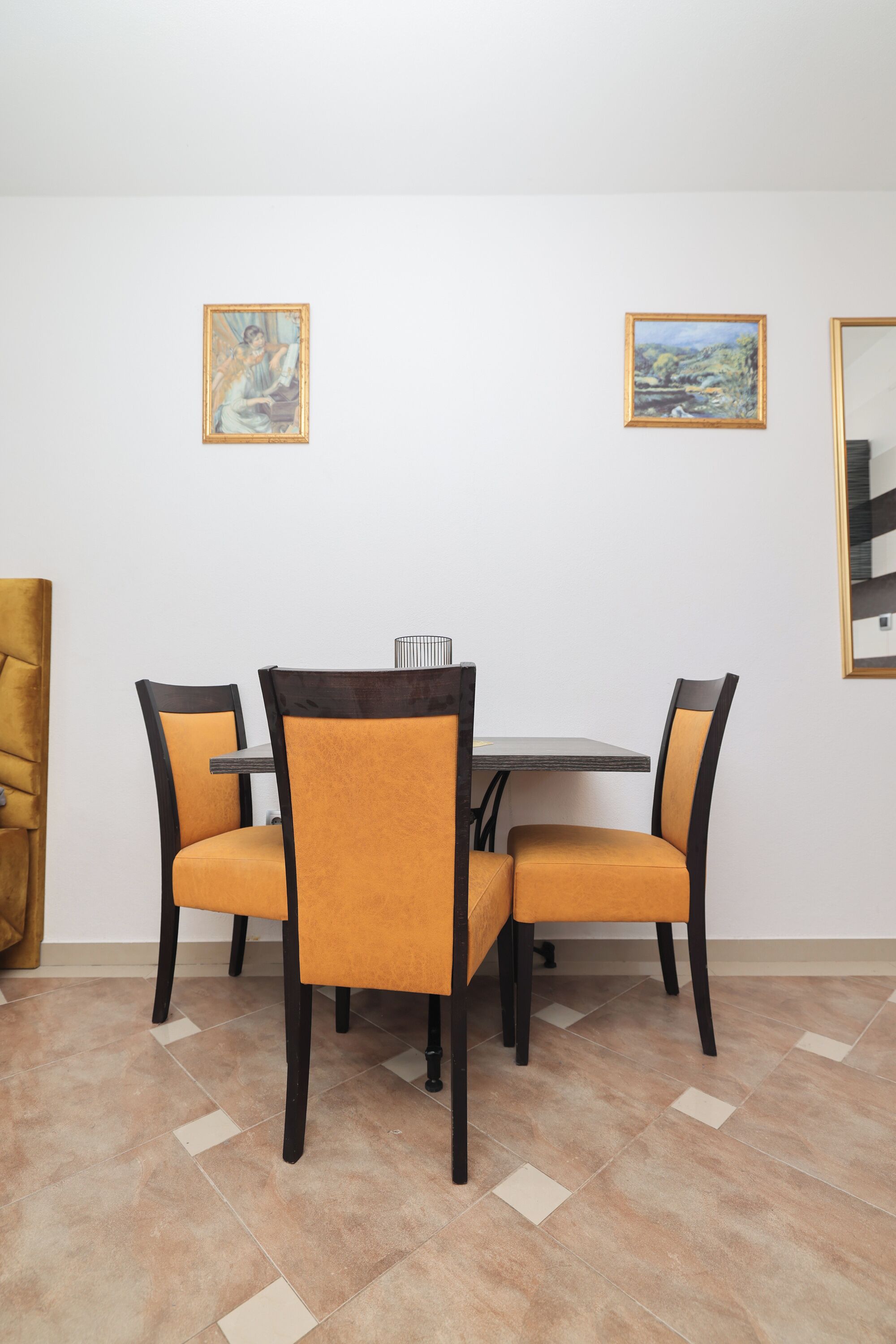 Uma sala de jantar com uma mesa e quatro cadeiras, duas pinturas emolduradas na parede e um chão estampado.
