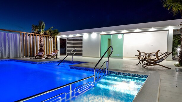 Piscina com interior azul, rodeada por espreguiçadeiras e uma vedação de madeira.