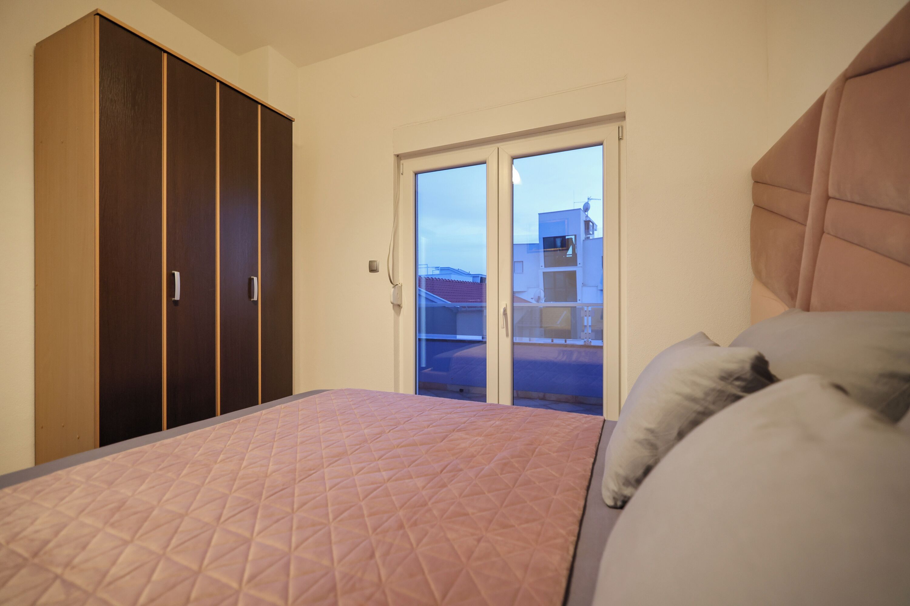 Quarto com uma cama, um guarda-roupa e uma porta de vidro deslizante que dá para uma varanda.