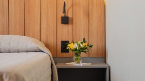 Quarto com cama, mesa de cabeceira com um vaso de flores e cabeceira de madeira.