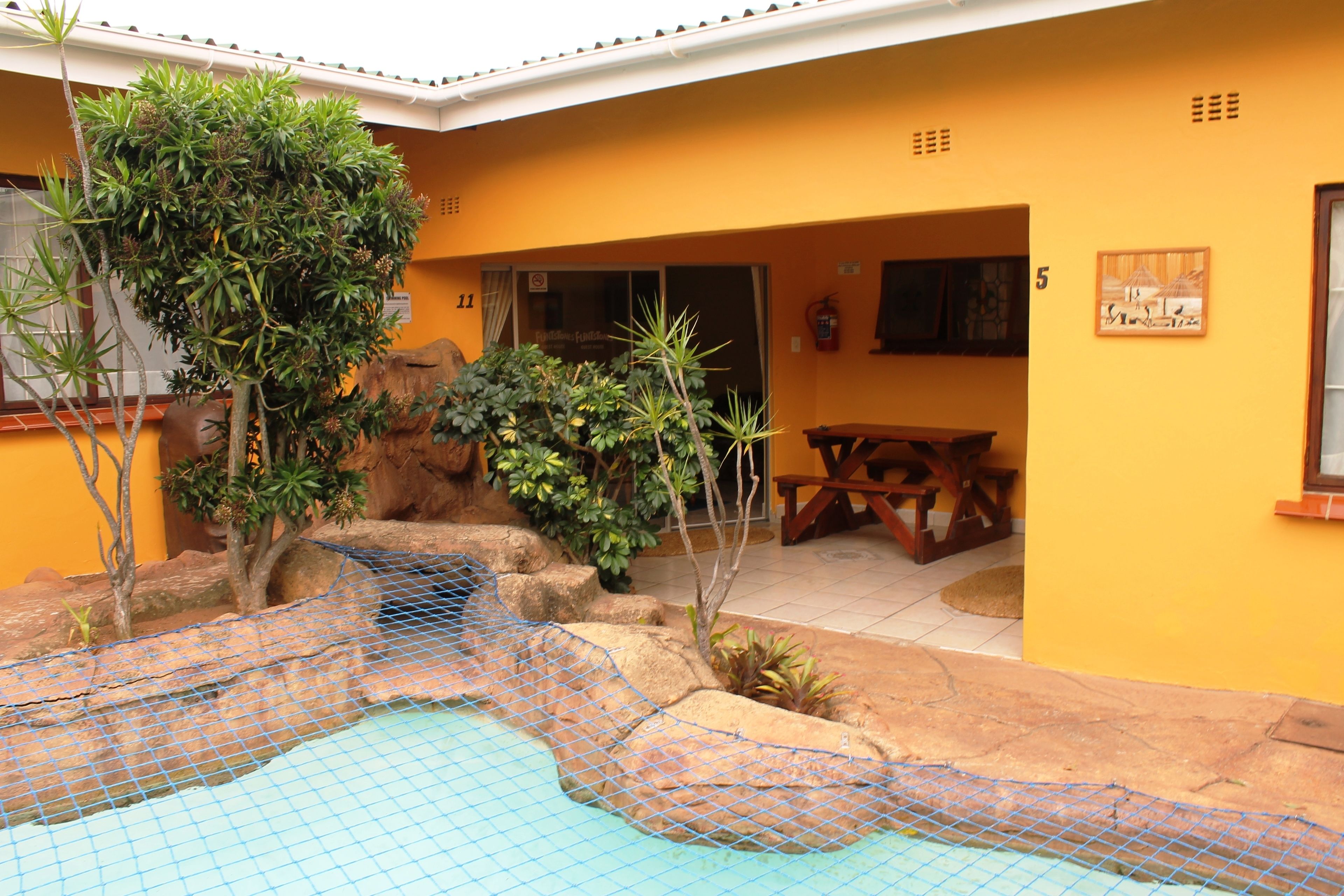 Um pátio com piscina, rodeado por plantas e uma mesa de madeira.