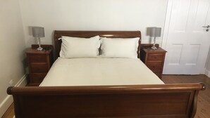 Cama de madeira com lençóis brancos em quarto com piso e paredes de madeira e branco.