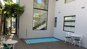 Uma área externa moderna com um deck de madeira, uma piscina pequena e móveis de jardim brancos.