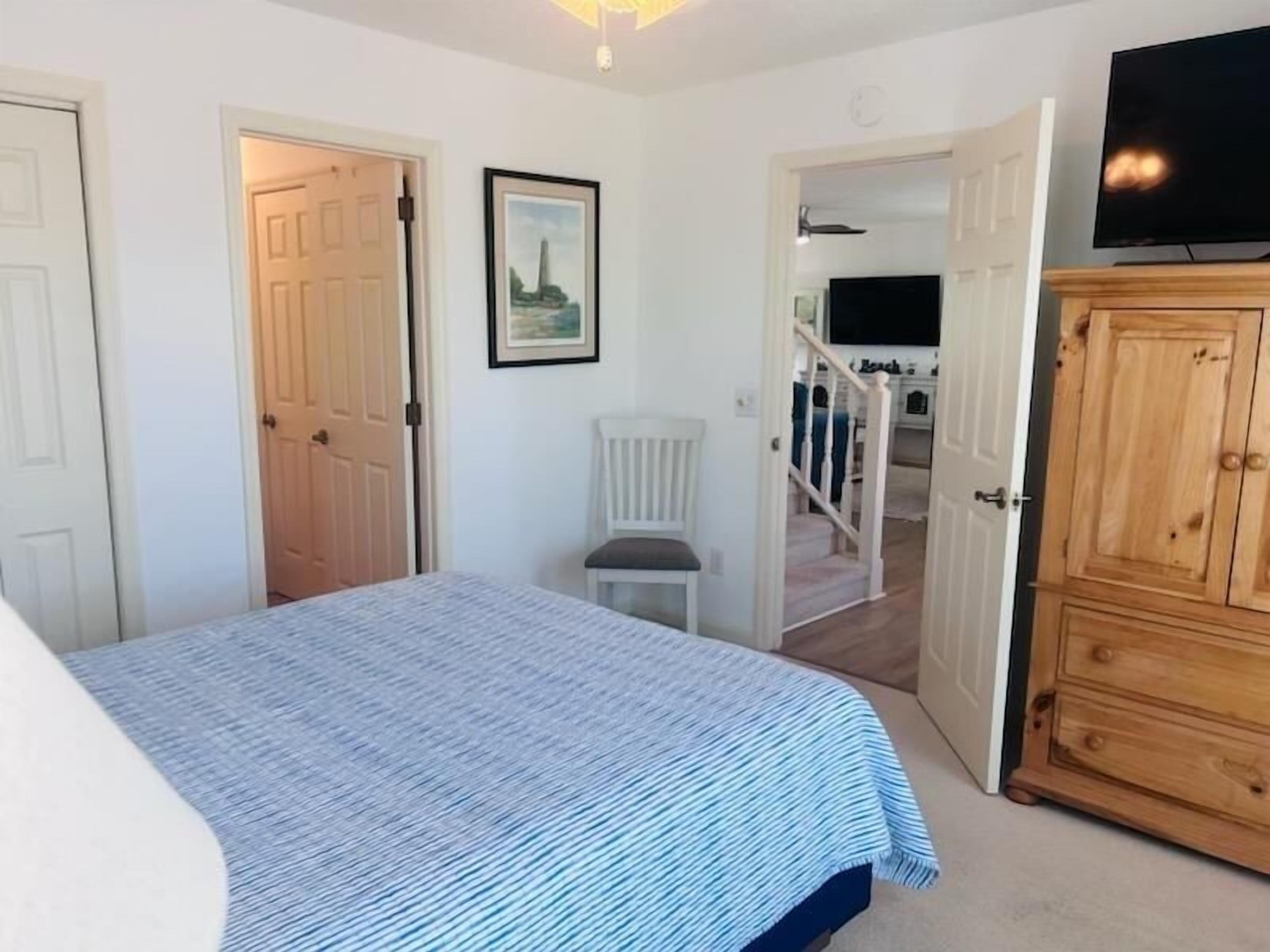 Quarto com cama, guarda-roupa de madeira, televisão e um quadro na parede.