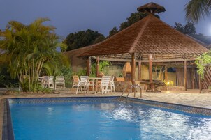 Uma área de piscina com borda revestida, um gazebo de madeira e assentos externos.