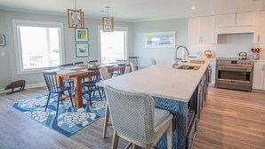 Cozinha moderna com uma ilha grande, armários brancos e um espaço de refeições com tapete estampado em azul.