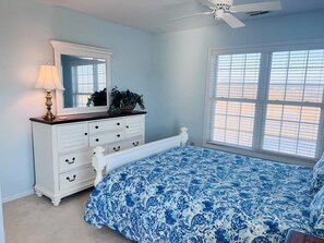 Um quarto com cama, penteadeira, espelho e janela.