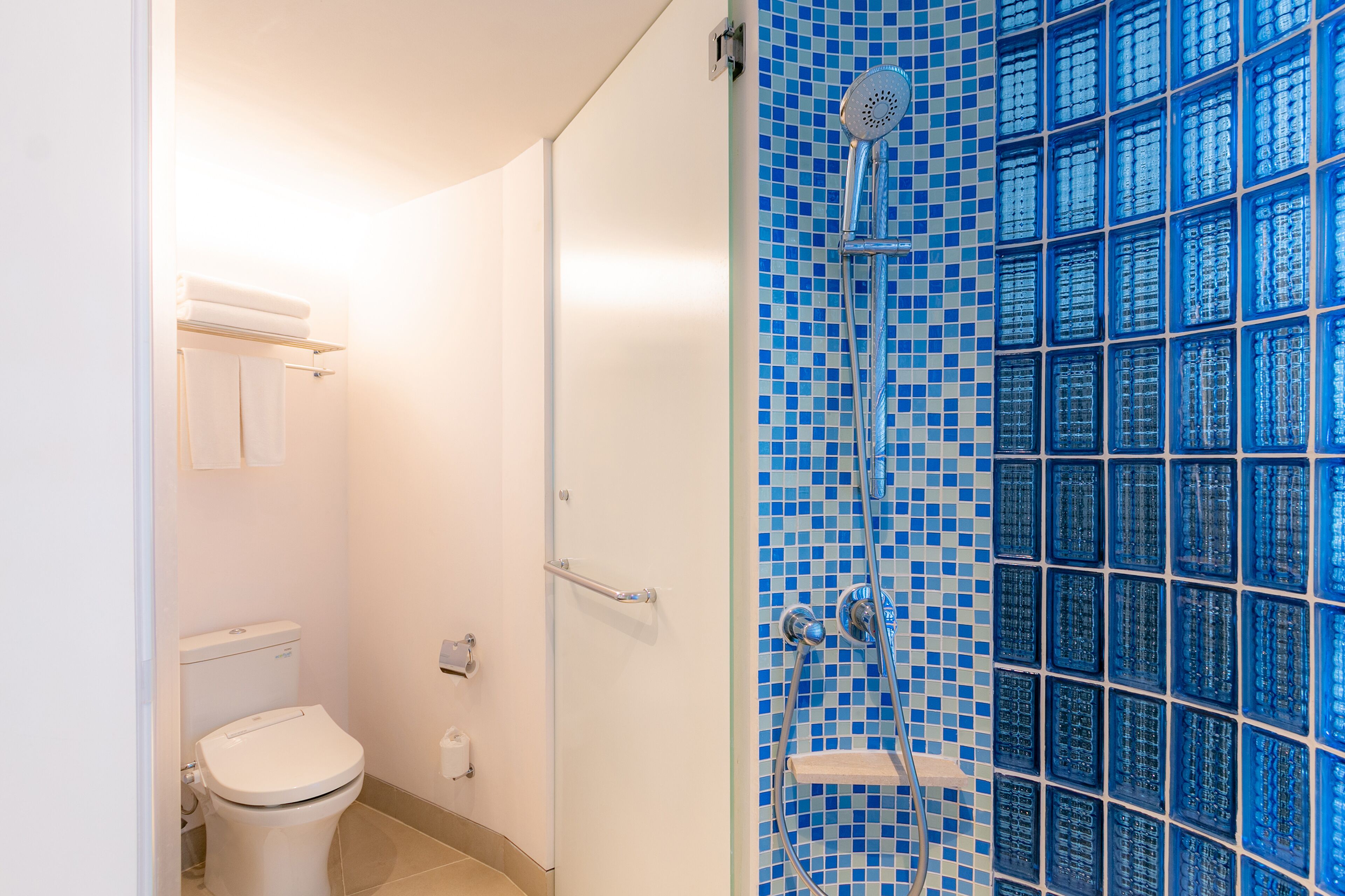 Casa de banho com sanita branca, cabine de duche em vidro e parede em mosaico azul.