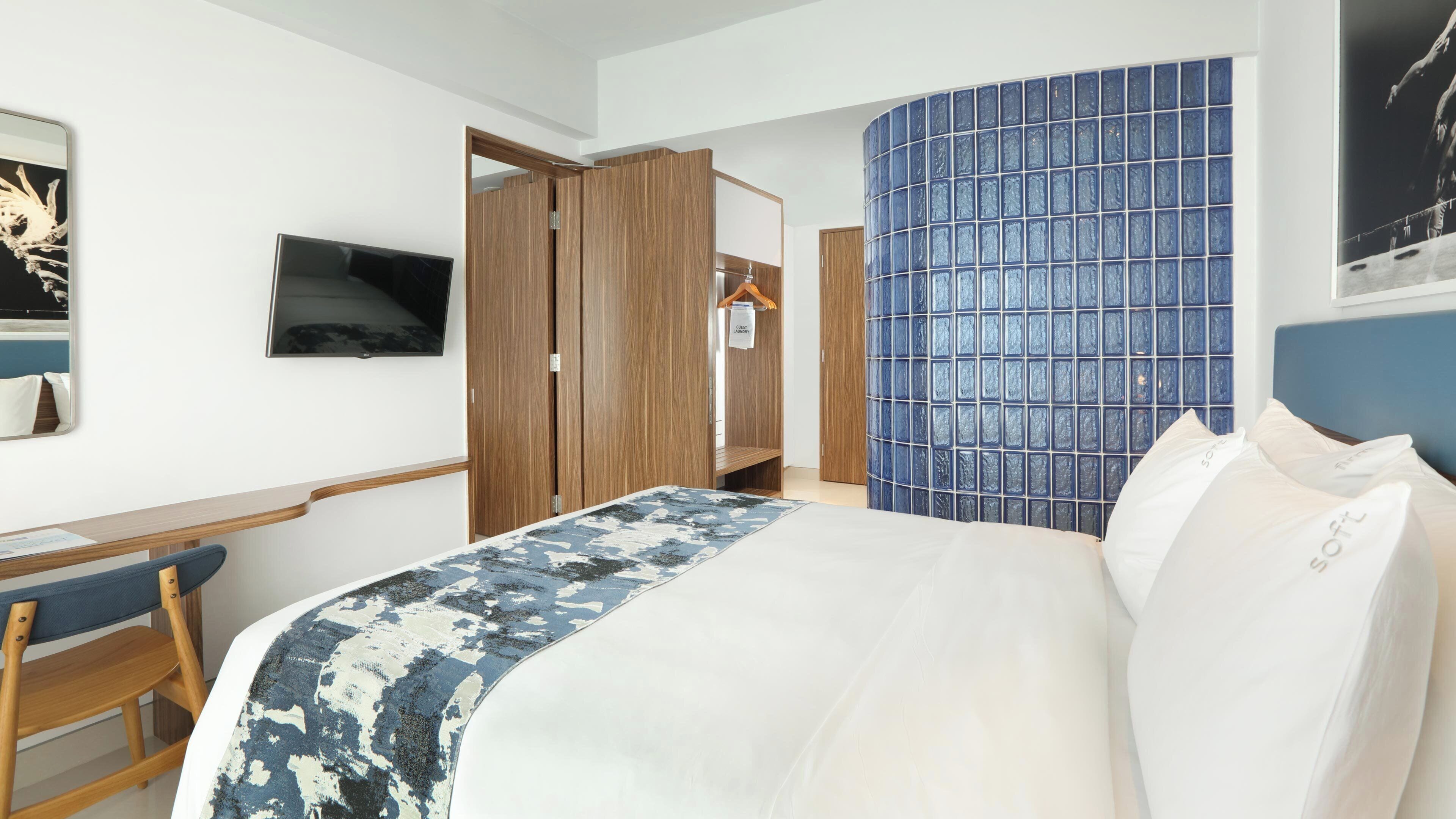 Quarto de hotel com cama, escrivaninha, televisão e guarda-roupa.
