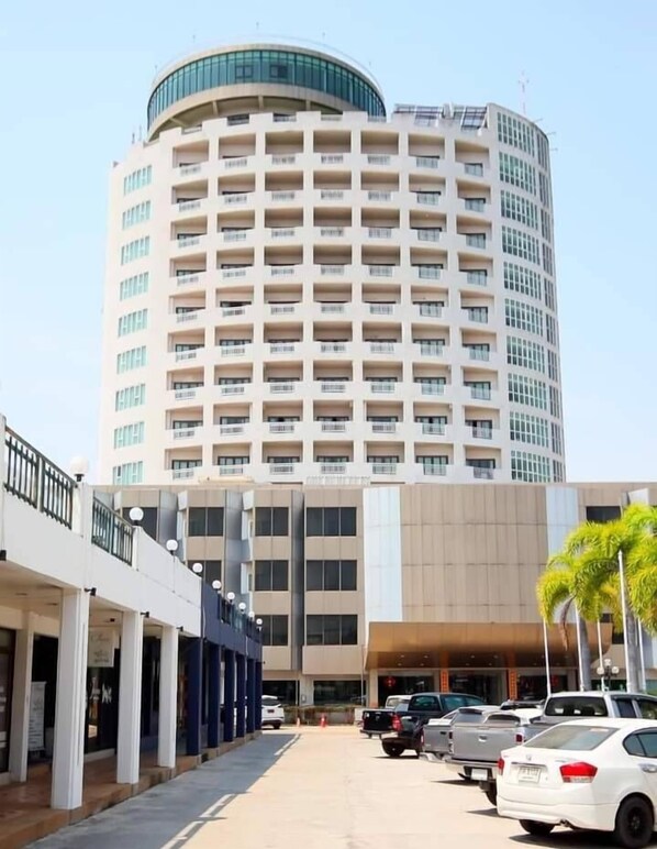 Um hotel com vários andares e átrio central, área de estacionamento com carros e um edifício com fachada curva.