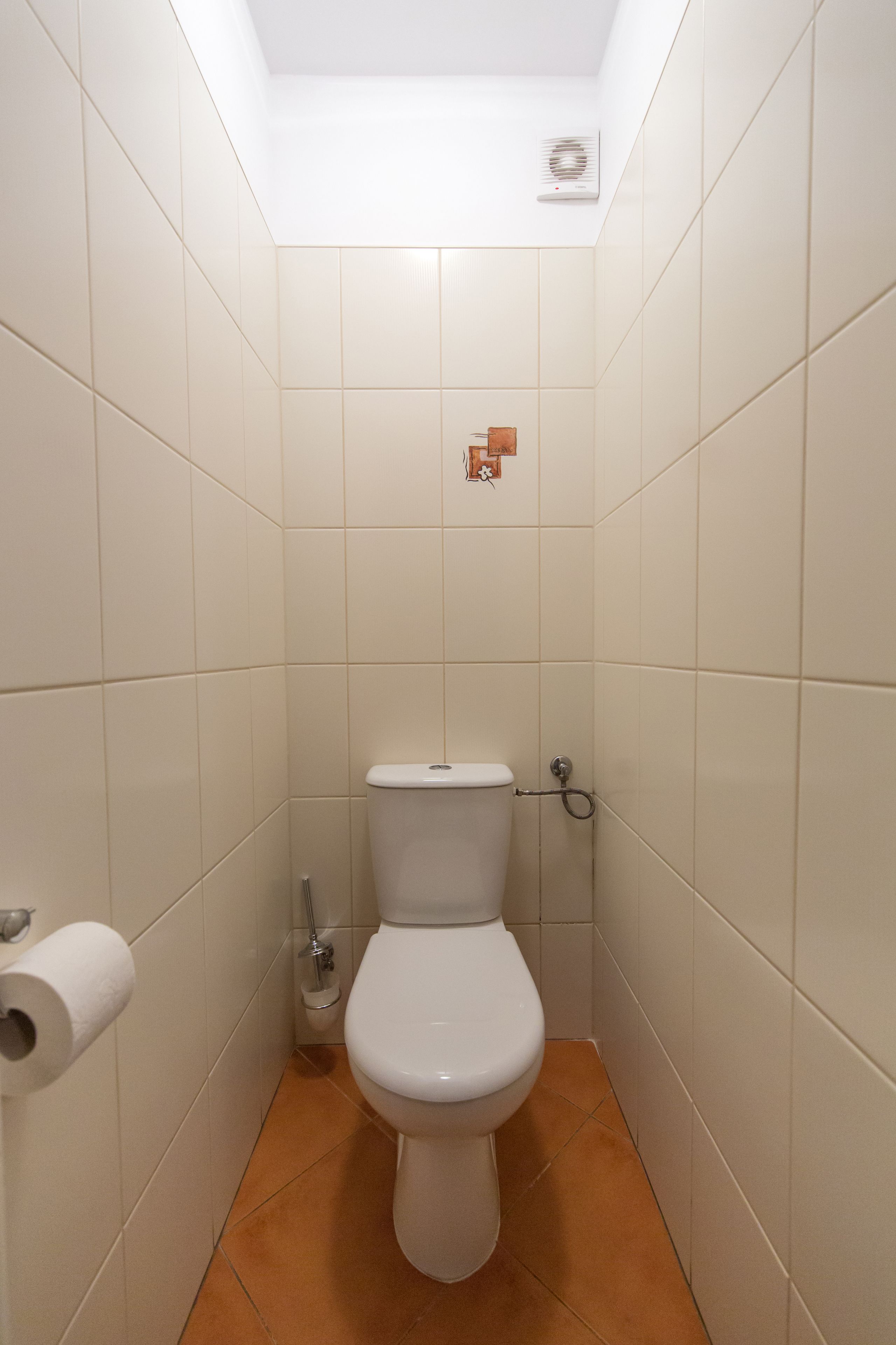 Um banheiro pequeno com azulejos, vaso sanitário branco, rolo de papel higiênico e chuveiro.