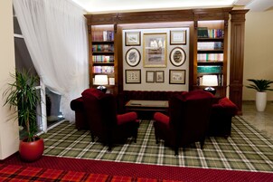 Uma biblioteca com poltronas vermelhas, carpete xadrez e estantes de livros.