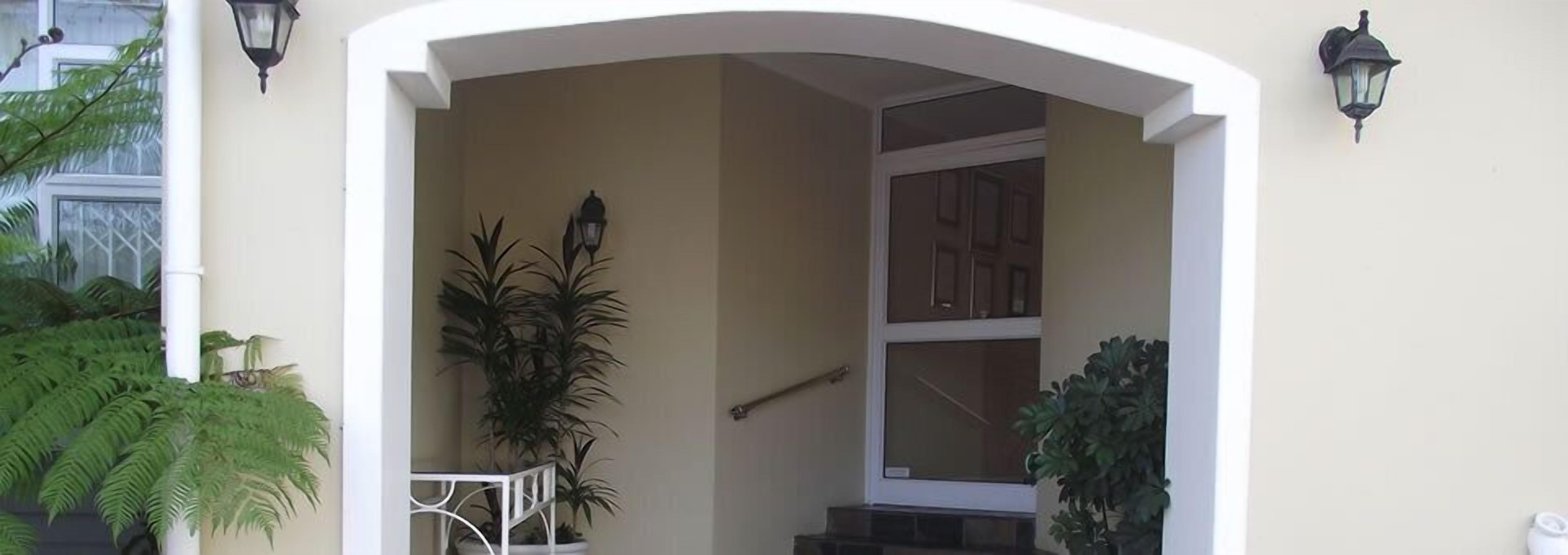 Entrada de edifício com arco branco, escadas e plantas em vasos.