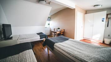 Quarto com duas camas de solteiro, uma escrivaninha com cadeira, radiador e guarda-roupa.