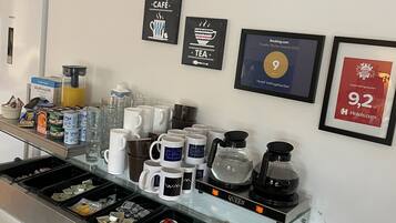 Uma mesa de café da manhã com opções de café e chá, uma geladeira e prêmios emoldurados na parede.