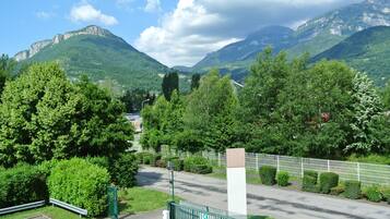 Uma área de estacionamento com cerca verde, um banco e uma estrada que leva a uma paisagem montanhosa.