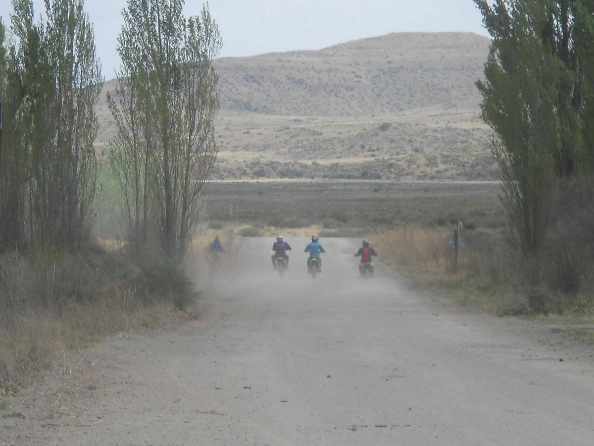 Uma estrada de terra com quatro motociclistas se afastando da câmera.