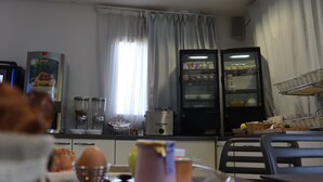 Cozinha equipada com frigorífico, micro-ondas e máquina de café. Há uma janela com cortinas e uma pia.