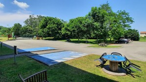 Uma área de estacionamento com mesa e cadeiras de piquenique, cercada por árvores e gramado.