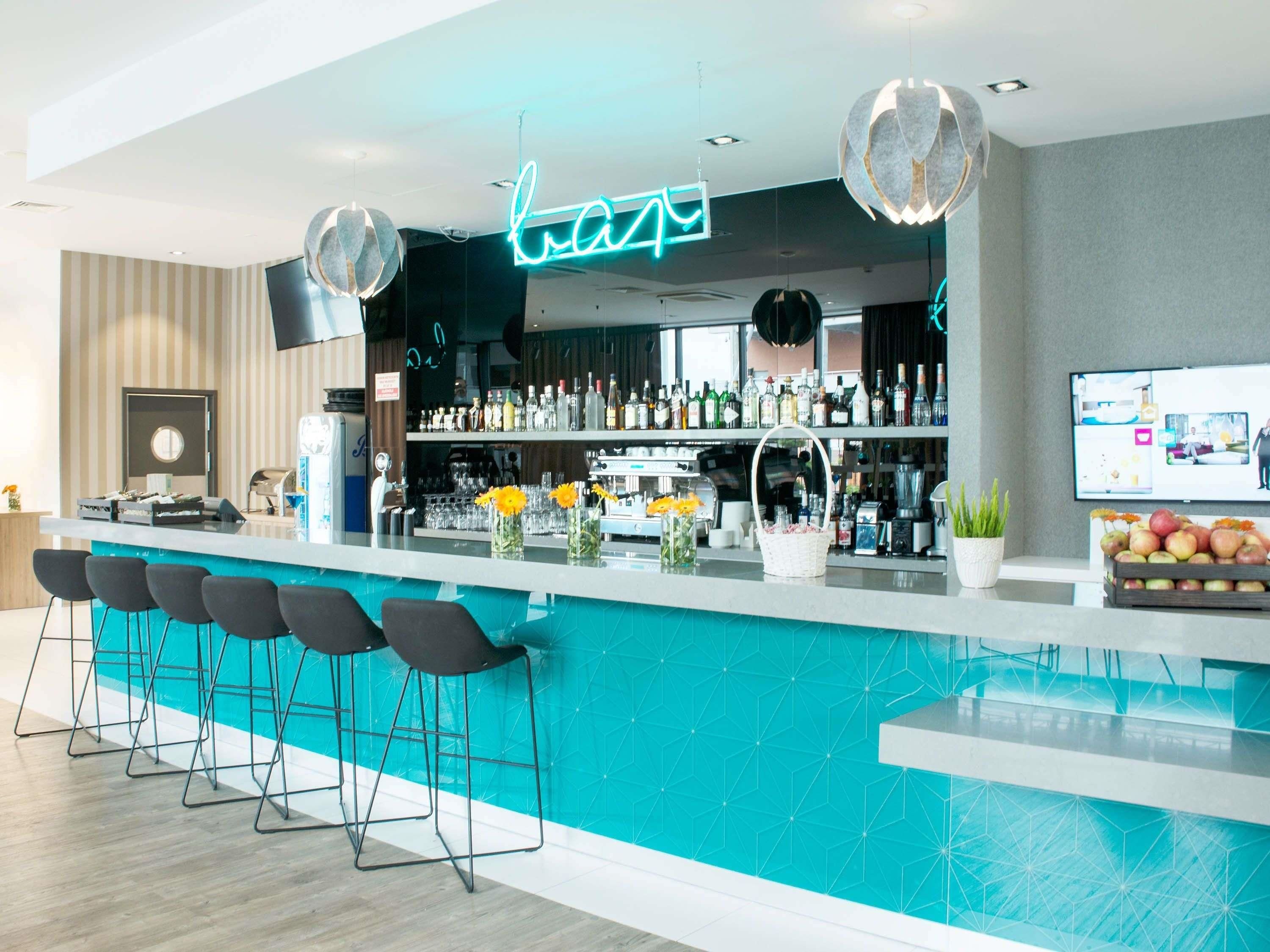 Uma área de bar moderna com uma placa de neon, banquetas, um balcão com garrafas e uma tela de televisão.