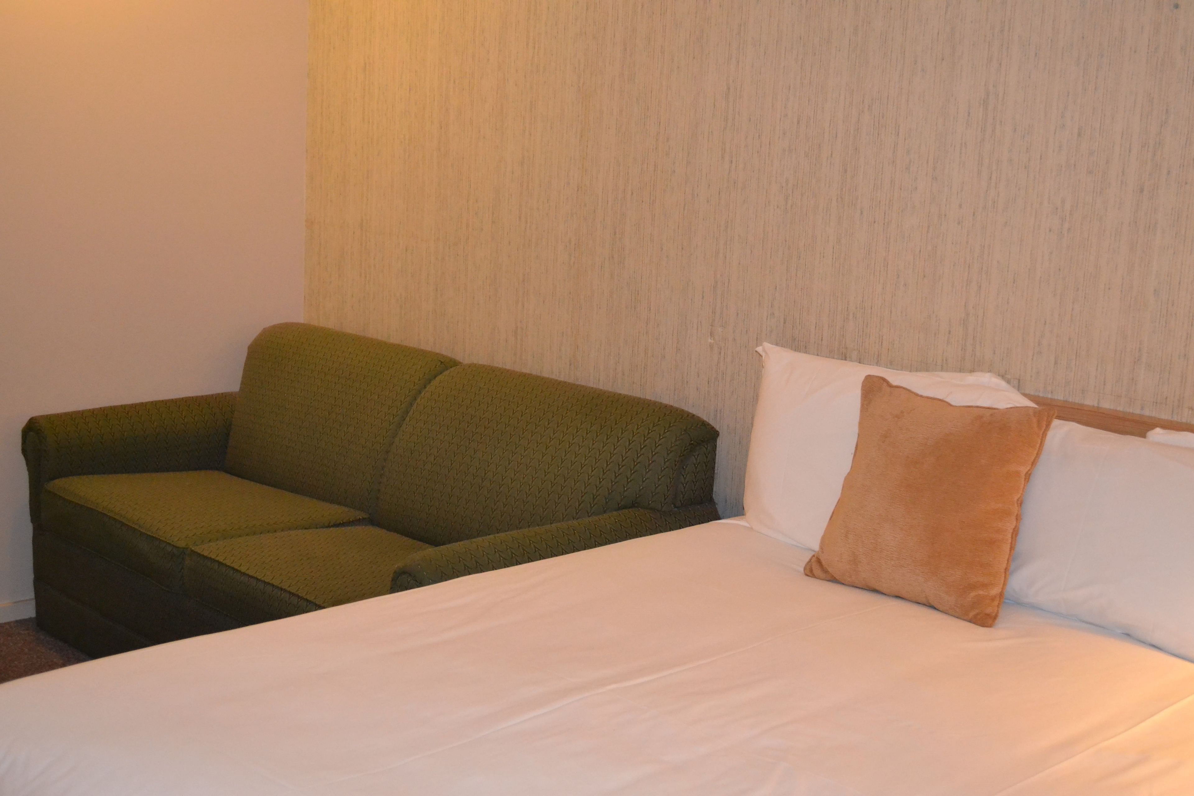 Quarto com cama, sofá verde e cabeceira de madeira.