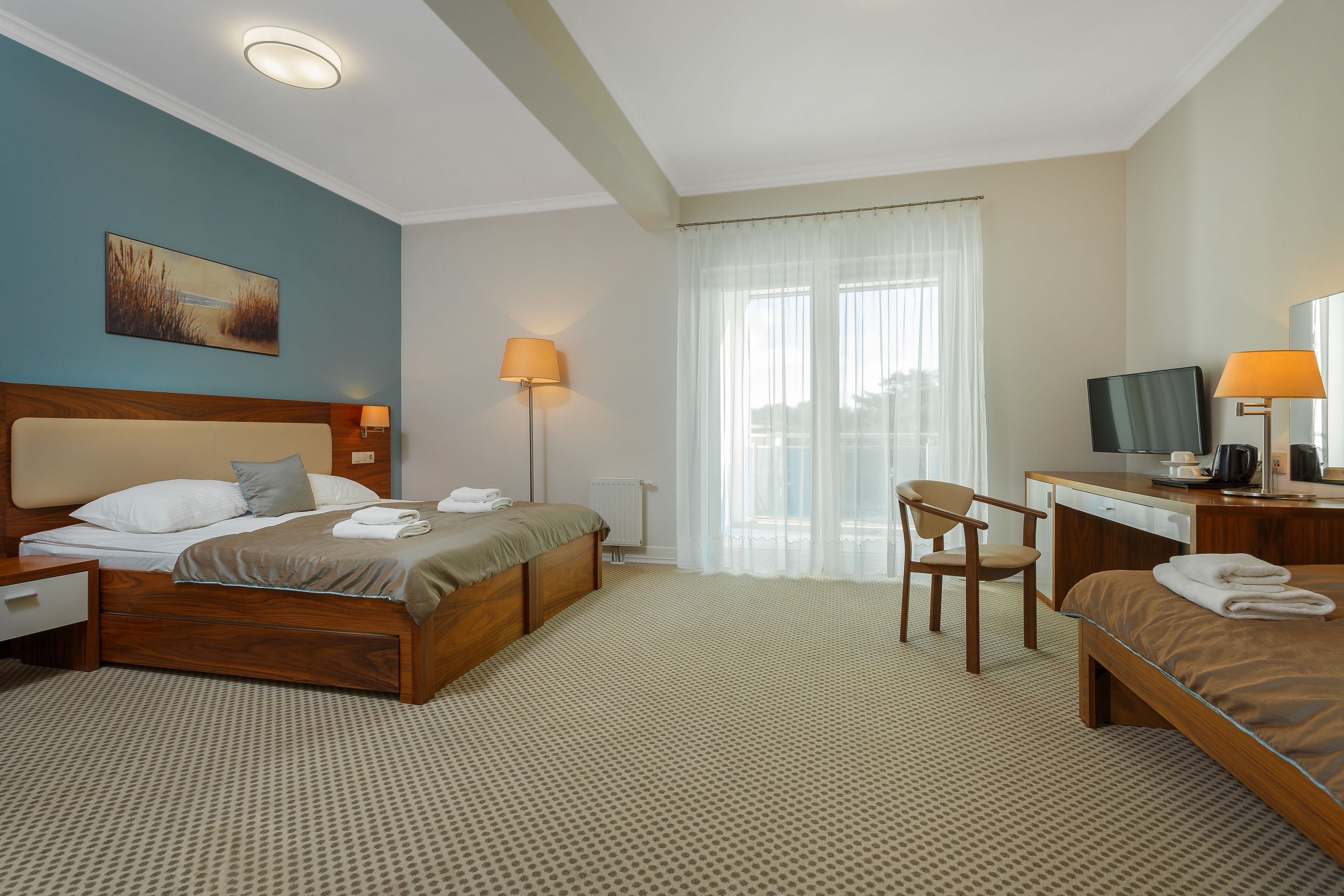 Quarto de hotel com cama, escrivaninha, cadeira, televisão e abajur.