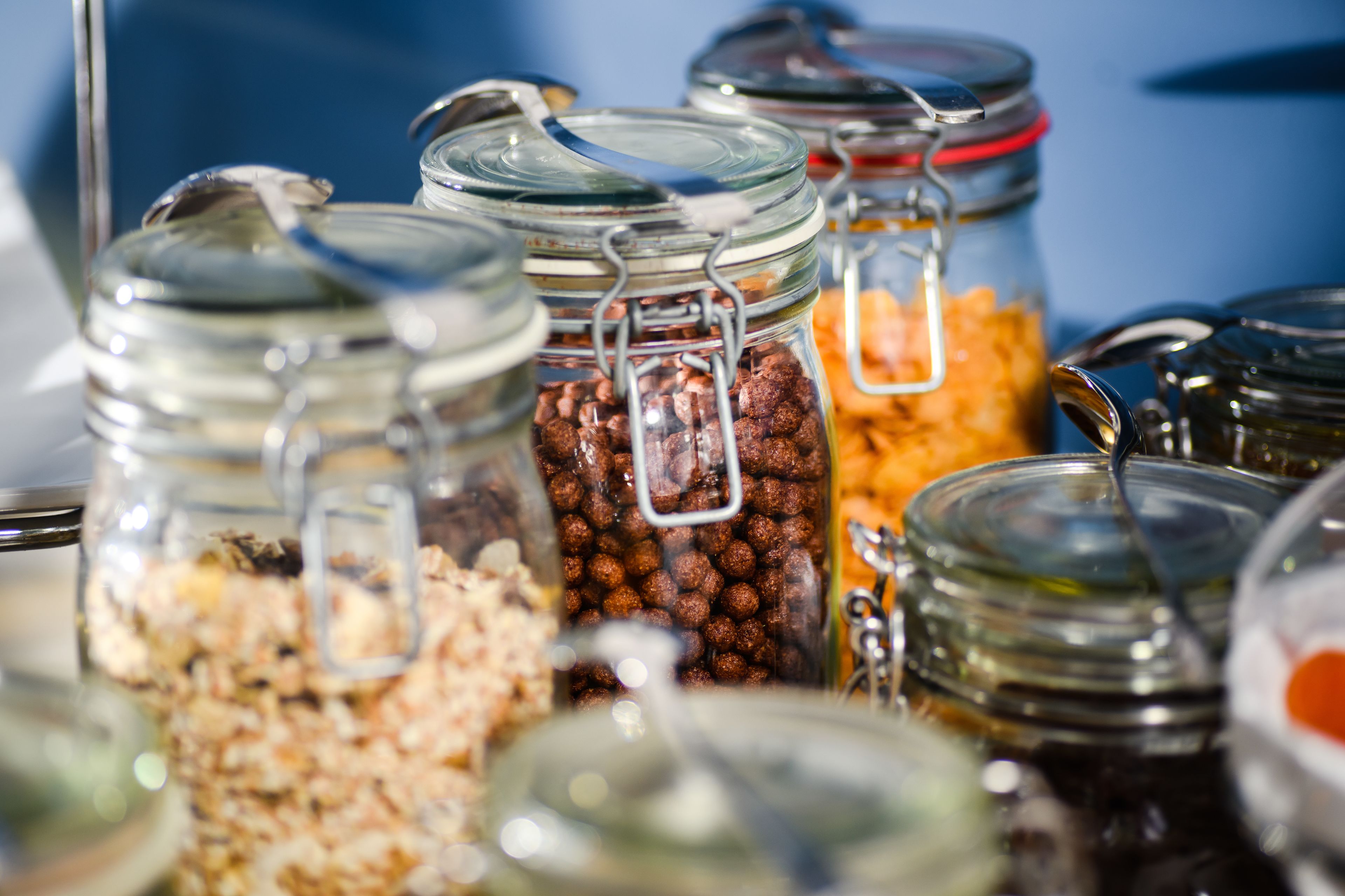 Diversos alimentos em recipientes de vidro com fechos metálicos, provavelmente em um buffet.