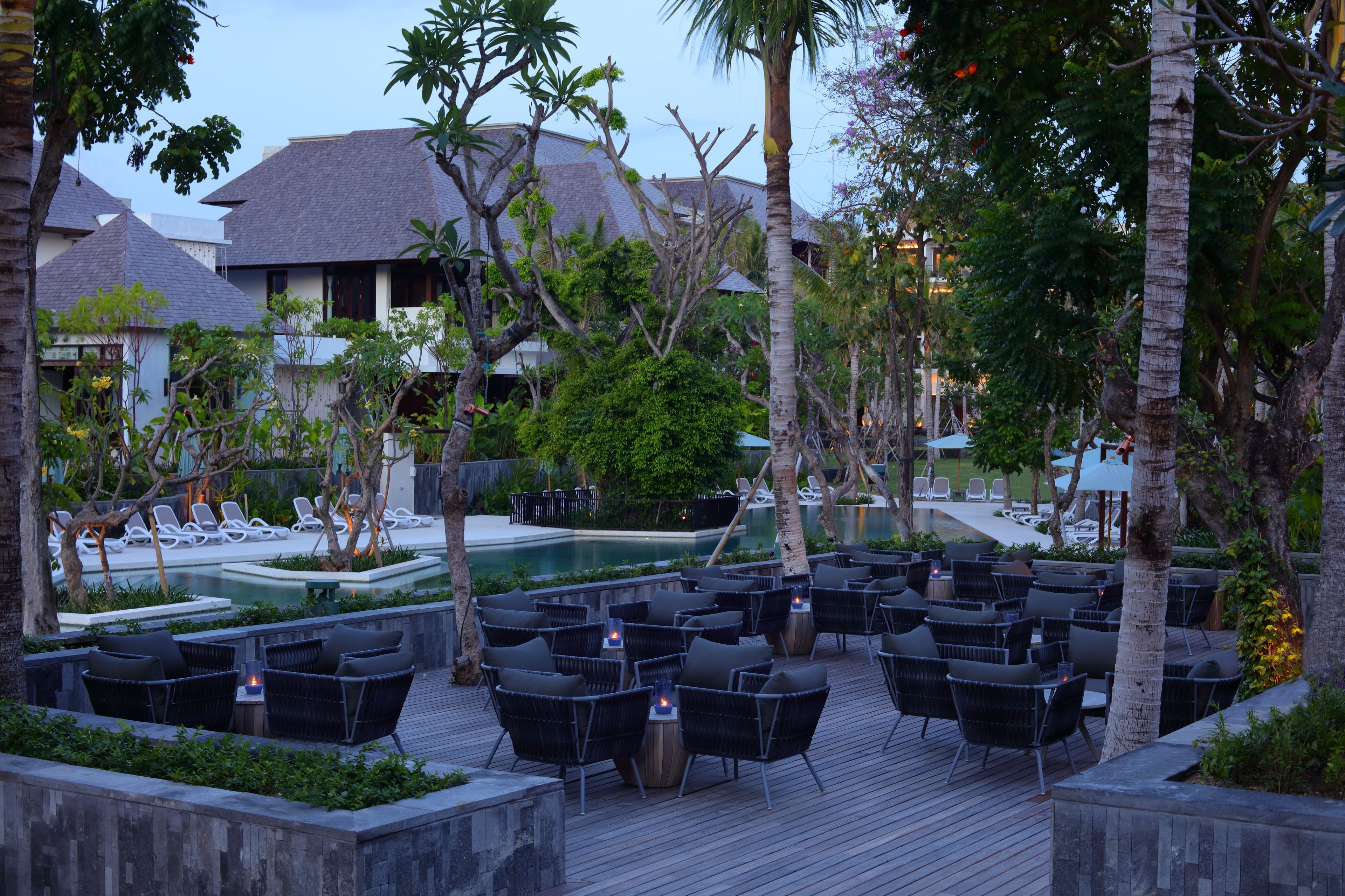 Resort com área de estar ao ar livre, piscina e paisagismo tropical.