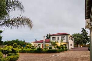 Uma casa de dois andares com telhado vermelho, cercada por sebes e árvores bem cuidadas.