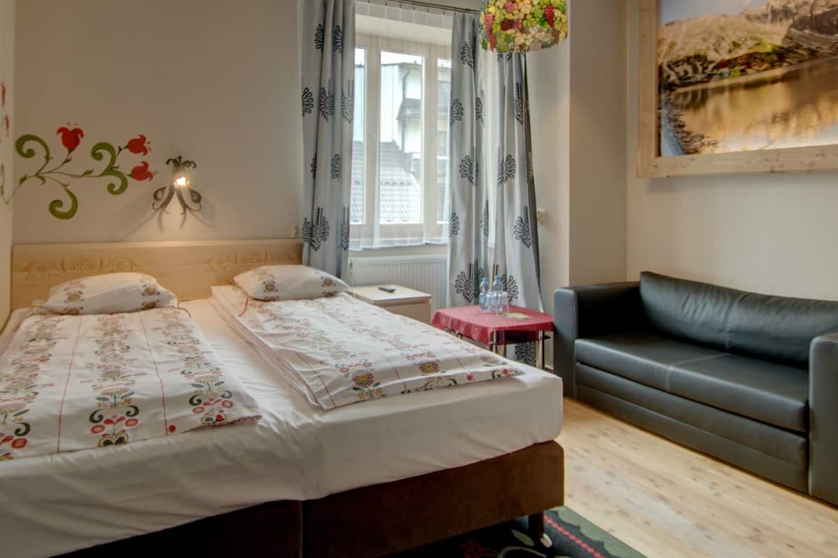 Quarto com cama, uma mesinha, sofá e janela com cortinas.