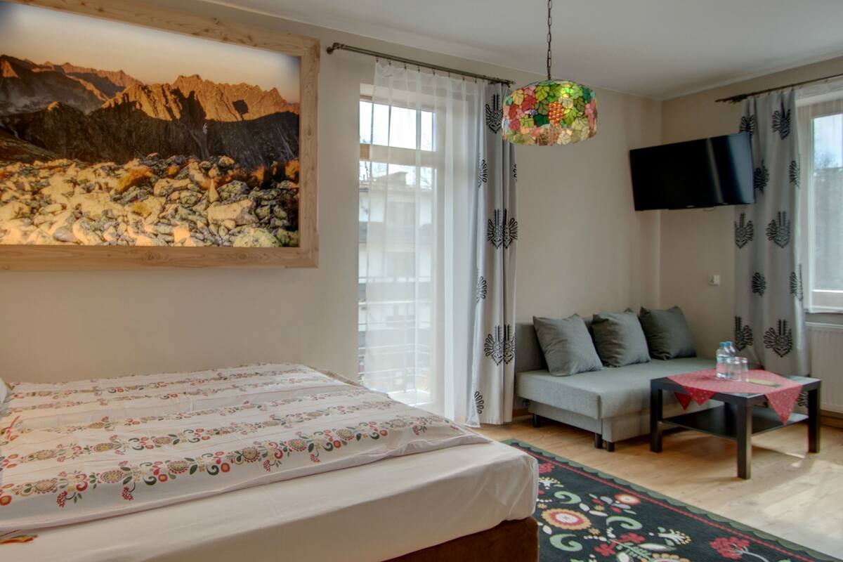 Quarto com cama, sofá, televisão e pintura de uma paisagem de montanhas.